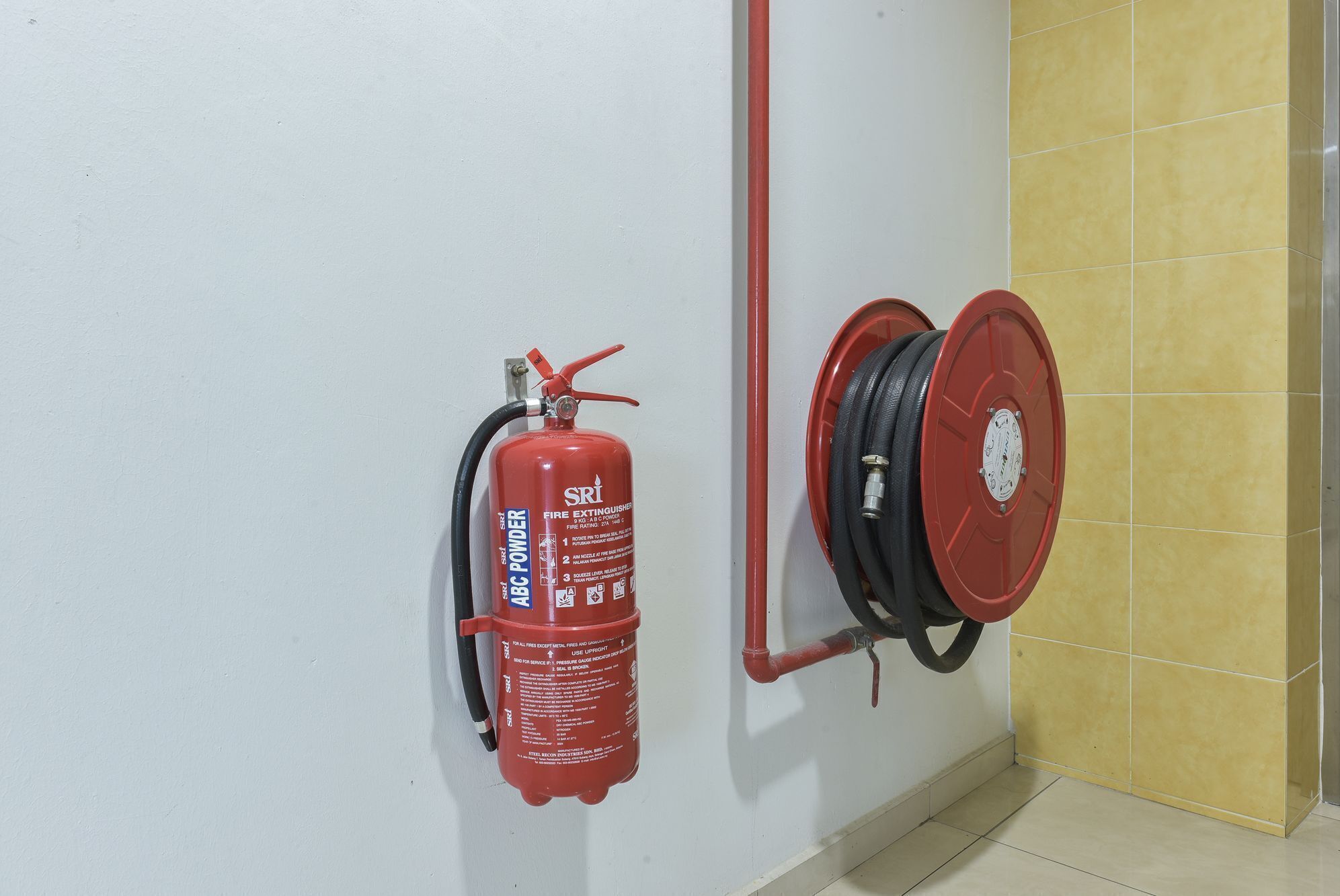 Um extintor fixado na parede ao lado de um carretel de mangueira vermelha.
