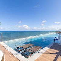 Área ao lado da piscina com espreguiçadeiras e vista para o oceano.