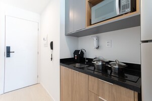 Cozinha moderna com bancada preta, armários de madeira, micro-ondas, máquina de café e chaleira.