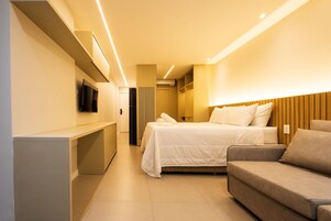 Quarto de hotel moderno com cama, sofá, televisão e closet espaçoso.