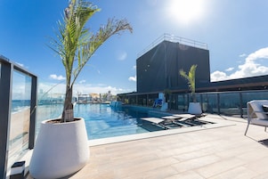 Piscina no terraço com vista para o oceano, uma grande planta em vaso e mobiliário de exterior moderno.