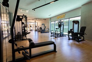 Uma academia com diversos equipamentos de ginástica, um banco e uma placa com a palavra 'SPORT'.