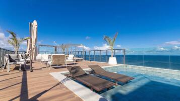 Um terraço com espreguiçadeiras, piscina e vista para o oceano.