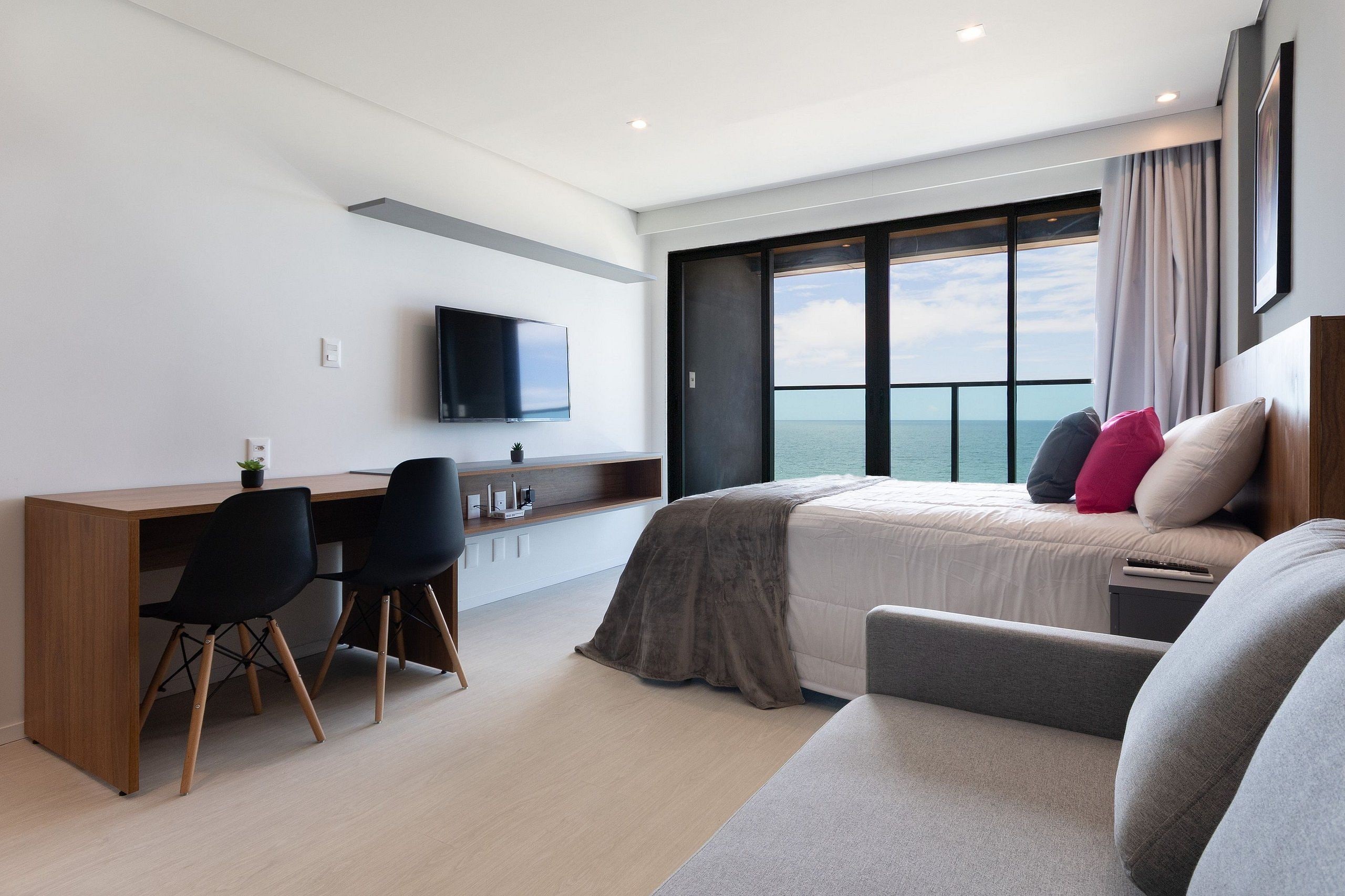 Quarto de hotel moderno com uma cama grande, uma escrivaninha e uma televisão.