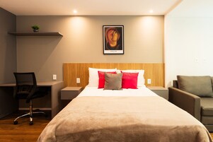 Quarto de hotel com cama, escrivaninha, cadeira e sofá.