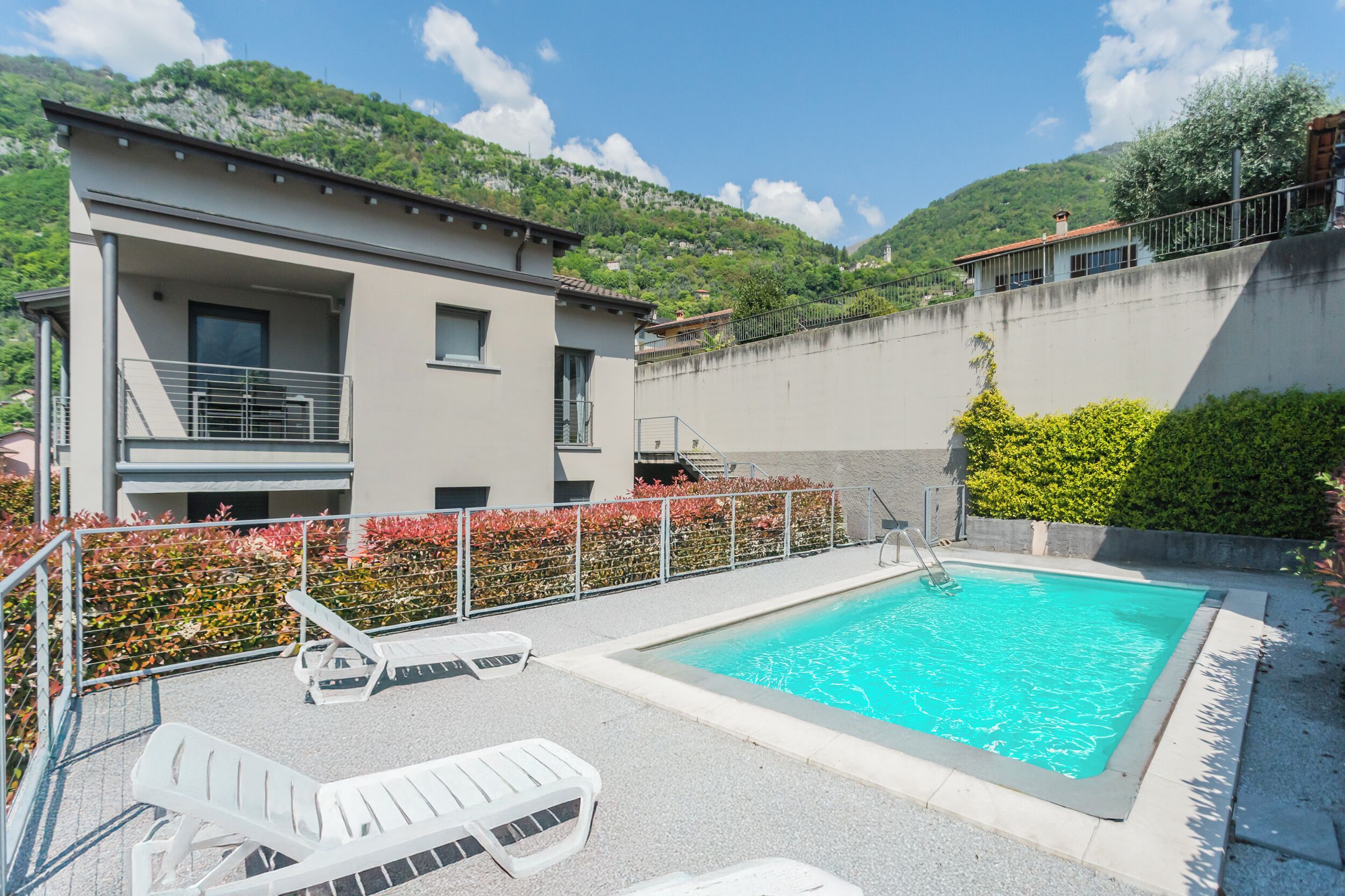 Uma área de piscina com espreguiçadeiras, um edifício com varandas e um cenário montanhoso ao fundo.