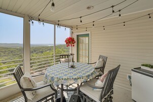 Uma área de estar coberta ao ar livre, com mesa e cadeiras, um arranjo floral pendente e vista para a paisagem.