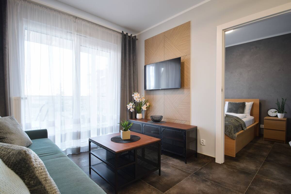 Uma sala de estar moderna com sofá, mesa de jantar, televisão fixada na parede e cama com cabeceira.