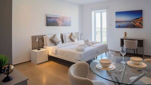 Quarto de hotel moderno com uma cama grande, uma escrivaninha e um espaço de refeições com mesa de vidro.