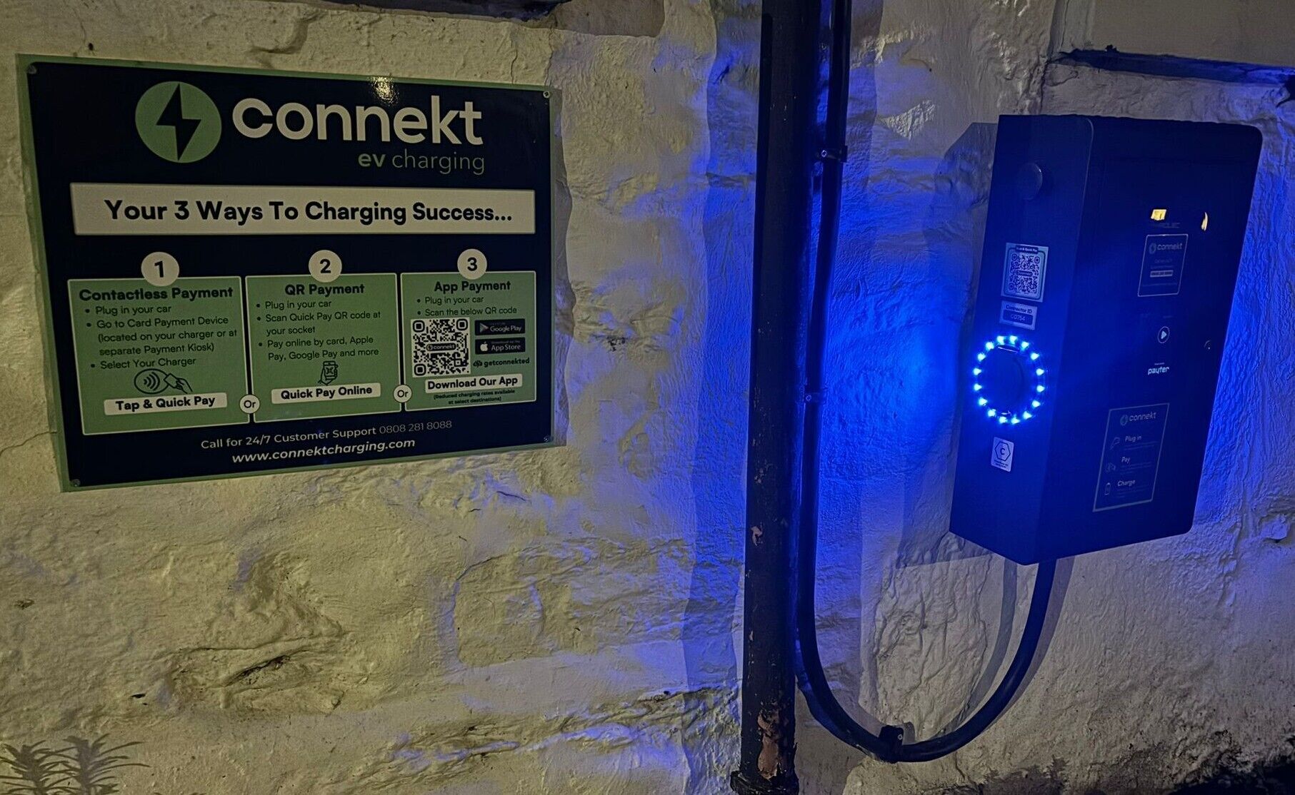 Uma estação de carregamento com um aviso detalhando três formas de pagamento: pagamento por aproximação, pagamento por QR code e pagamento via aplicativo.