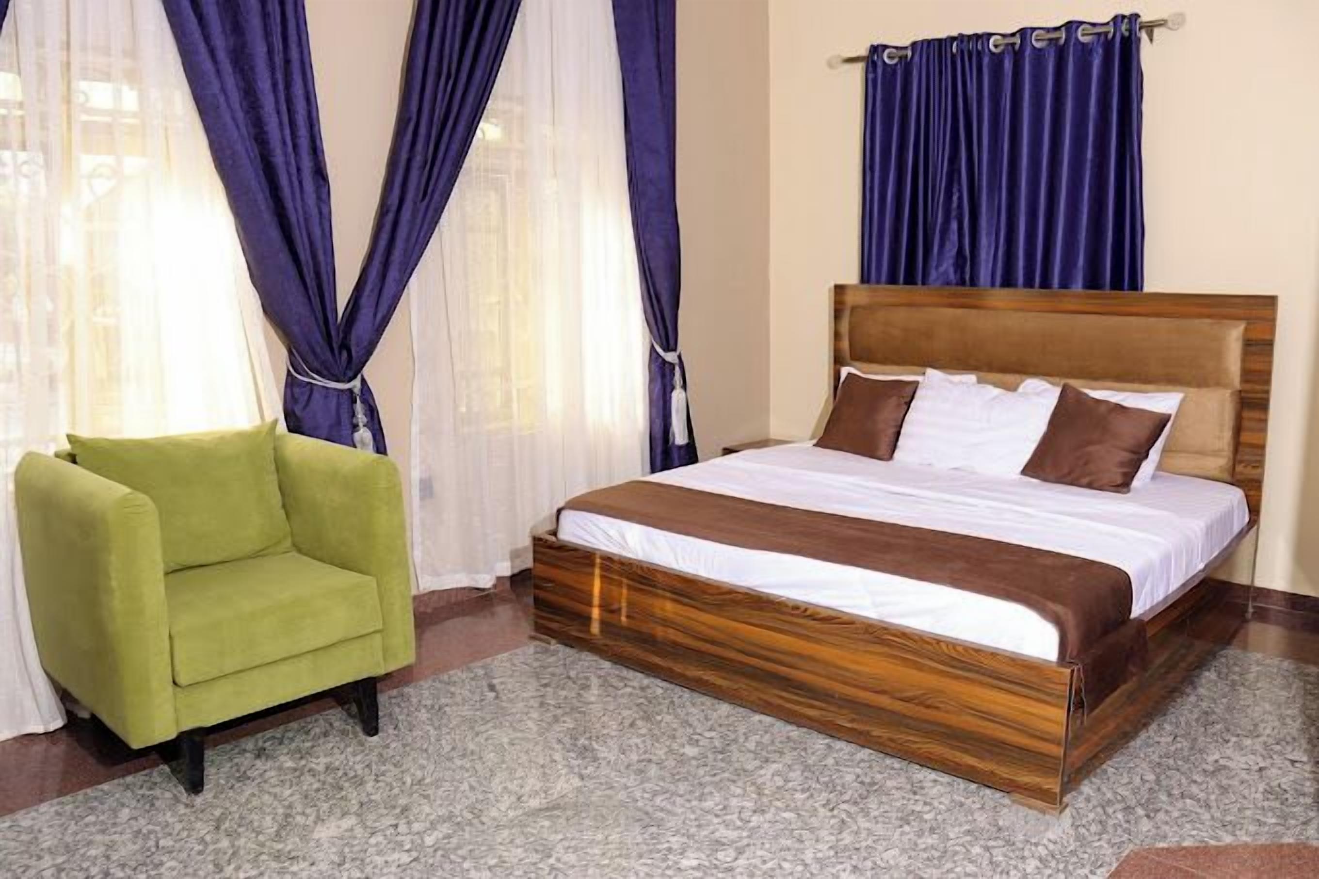Quarto com cama de madeira, poltrona verde e cortinas azuis.