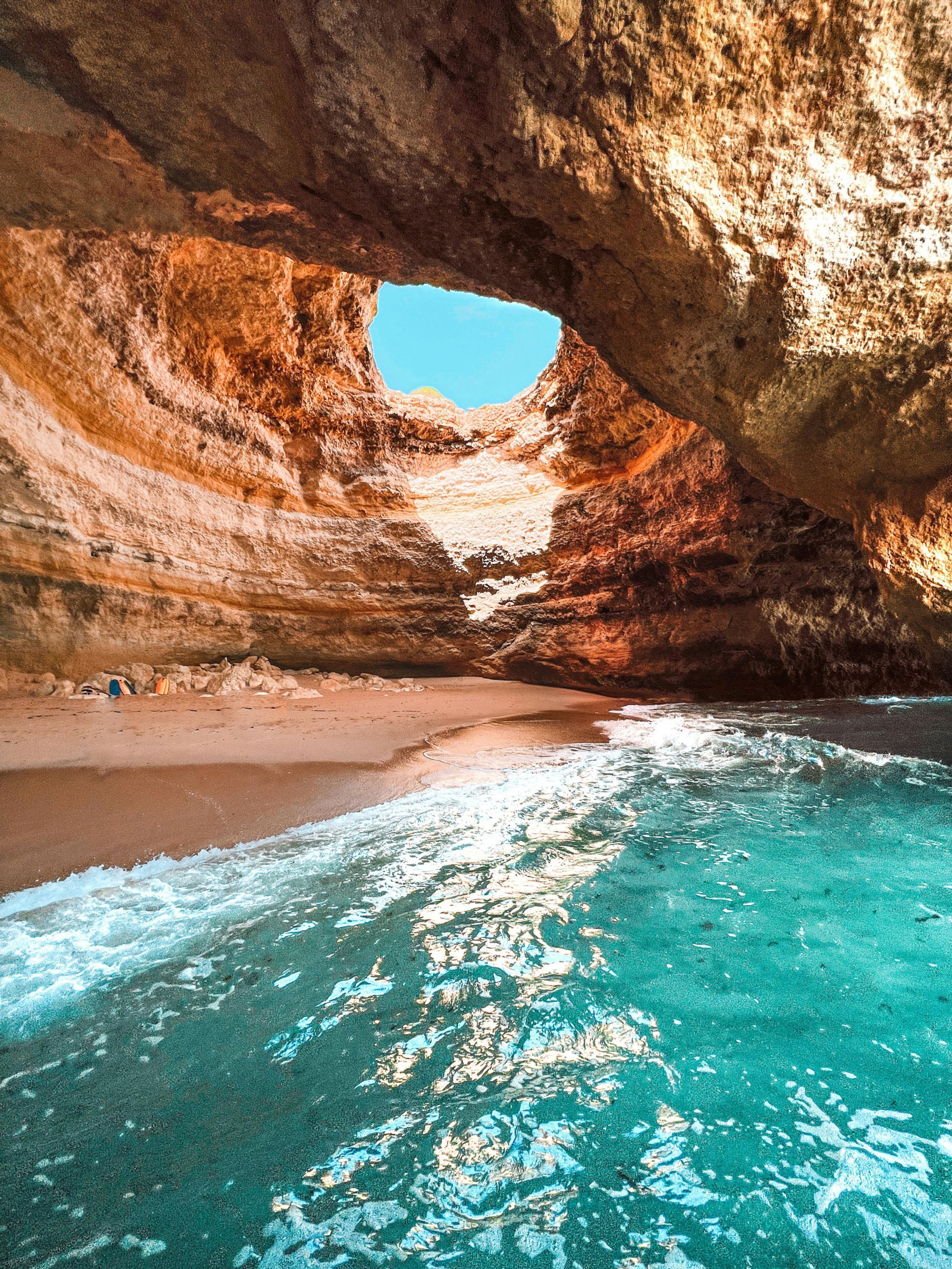 Formação rochosa natural com uma abertura de caverna para uma praia e águas turquesa cristalinas.