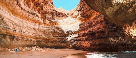 Formação rochosa natural com uma abertura de caverna para uma praia e águas turquesa cristalinas.