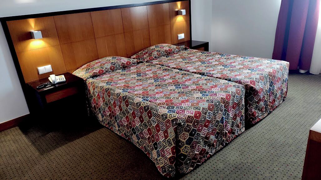 Quarto de hotel com duas camas, cabeceira de madeira, abajures e telefone na mesinha de cabeceira.