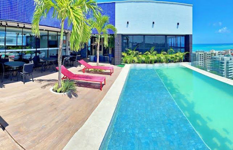 Um hotel moderno com piscina no terraço, espreguiçadeiras e palmeiras.