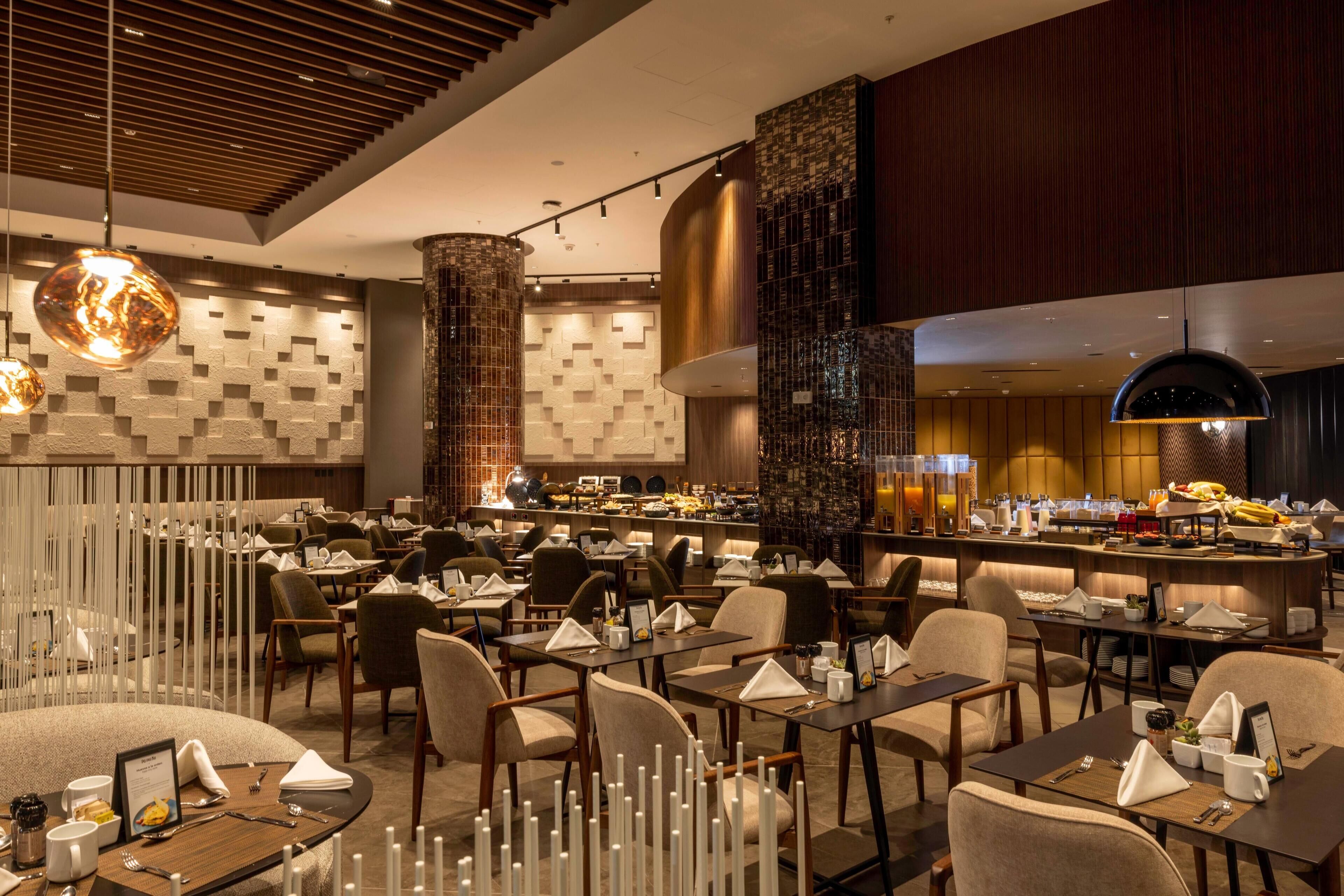 Restaurante moderno com diversas opções de assentos, incluindo mesas e cabines, e um buffet com variedade de alimentos.