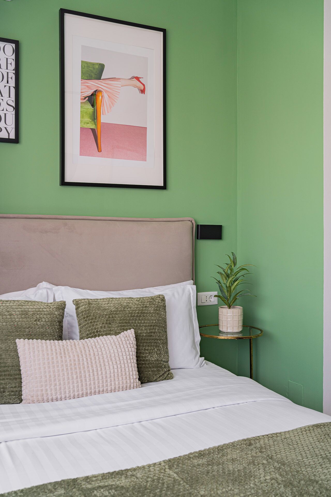 Cama bem arrumada com cabeceira verde, roupa de cama branca e travesseiros verdes e brancos. Um quadro emoldurado está pendurado na parede acima da cama.