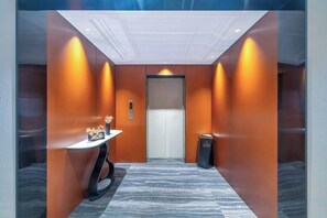 Corredor com balcão de recepção, lixeira e elevador.