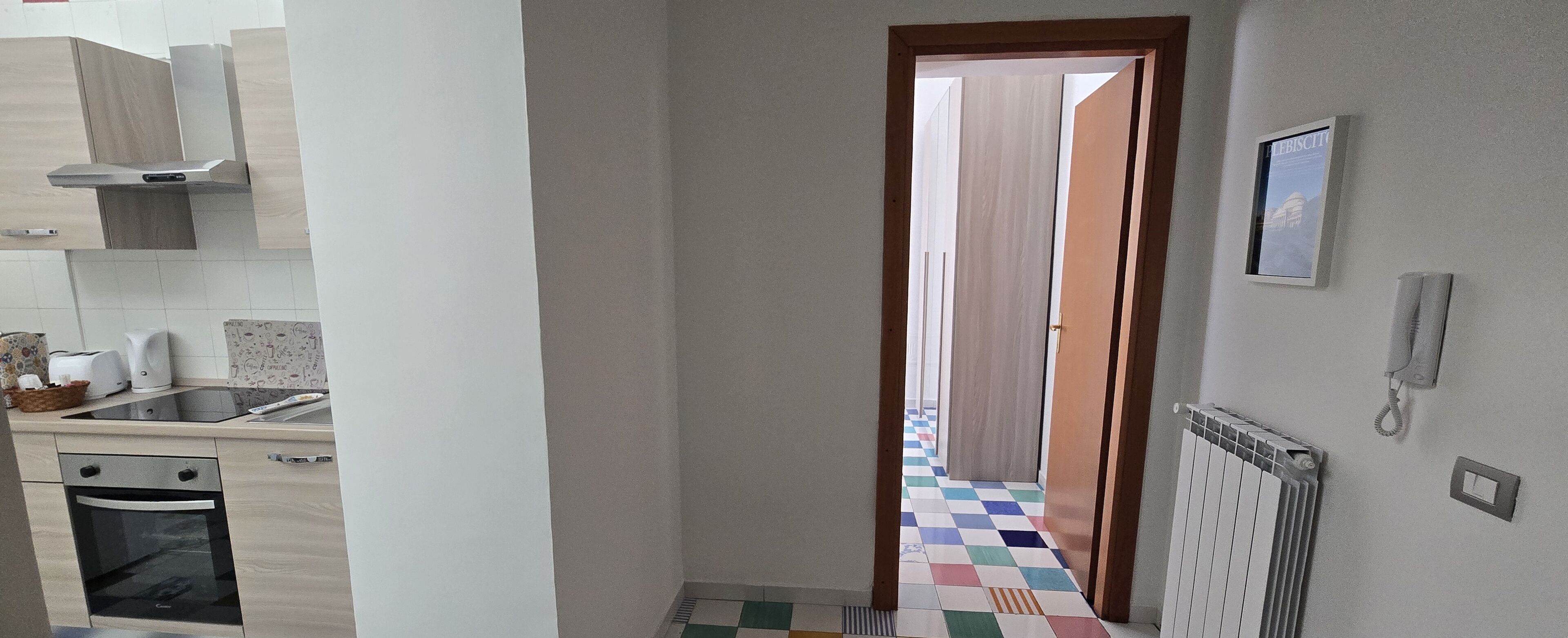 Um corredor estreito com chão xadrez, um radiador e um telefone na parede.
