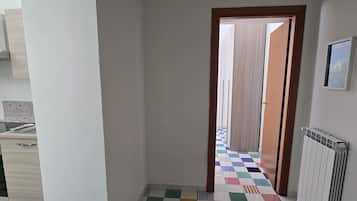 Um corredor estreito com chão xadrez, um radiador e um telefone na parede.