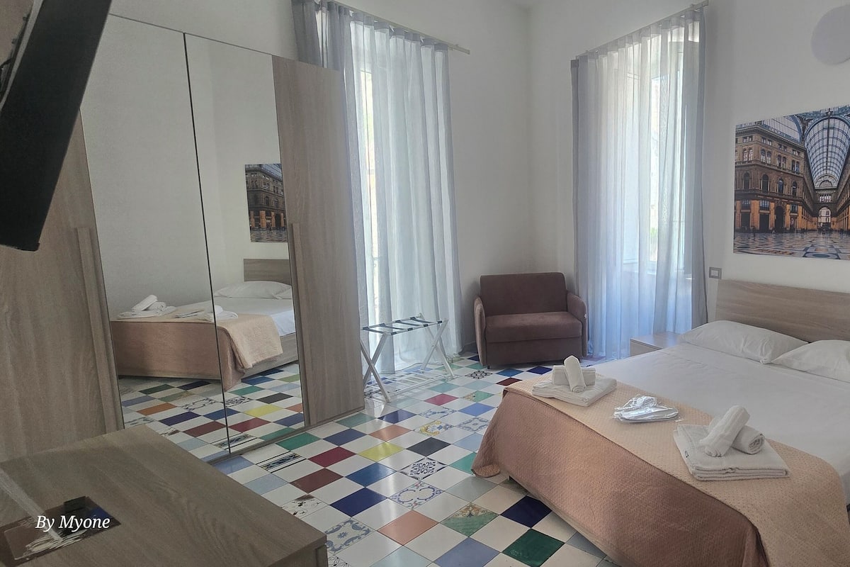Quarto de hotel com uma cama grande, uma cadeira, um espelho e um quadro na parede.