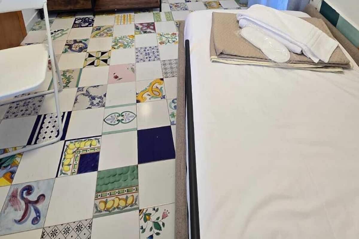 Quarto de hotel com cama, escrivaninha, cadeira, televisão e banheiro visível por uma porta aberta.