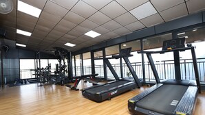 Academia com esteiras, um banco de musculação e um ventilador.