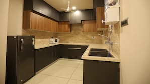 Cozinha com armários escuros, micro-ondas, geladeira, pia e ventilador de teto.