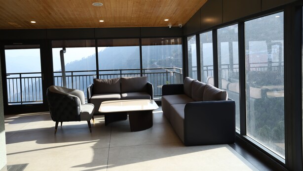 Uma sala de estar moderna com teto de madeira, janelas amplas e uma varanda com vista para uma paisagem montanhosa.
