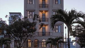 Um hotel com vários andares, varandas, uma loja boutique no térreo e um jardim bem cuidado.
