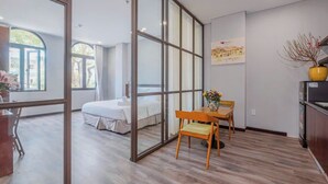 Quarto de hotel moderno com uma grande porta de vidro deslizante para uma varanda, uma cama, uma mesa de jantar com cadeiras e uma área de cozinha.