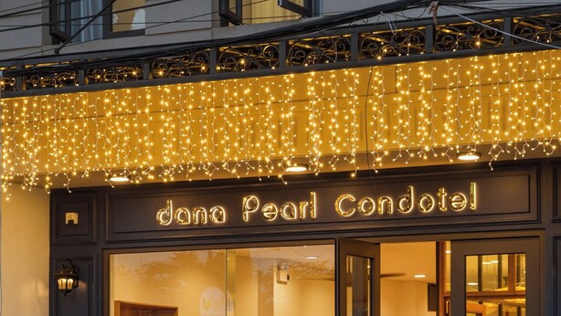 Exterior do Dana Pearl Condotel, com fachada escura, grandes janelas de vidro e uma placa sobre a entrada.