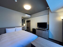 Quarto de hotel com uma cama grande, televisão de tela plana, escrivaninha com computador, guarda-roupa e ar-condicionado.