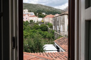 Vista da janela mostrando uma encosta com edifícios, árvores e telhado de telhas vermelhas.
