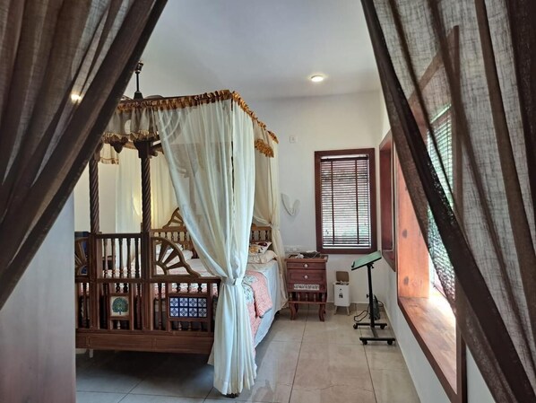 Quarto com cama de dossel, mesa de cabeceira, cômoda e janela com persianas.