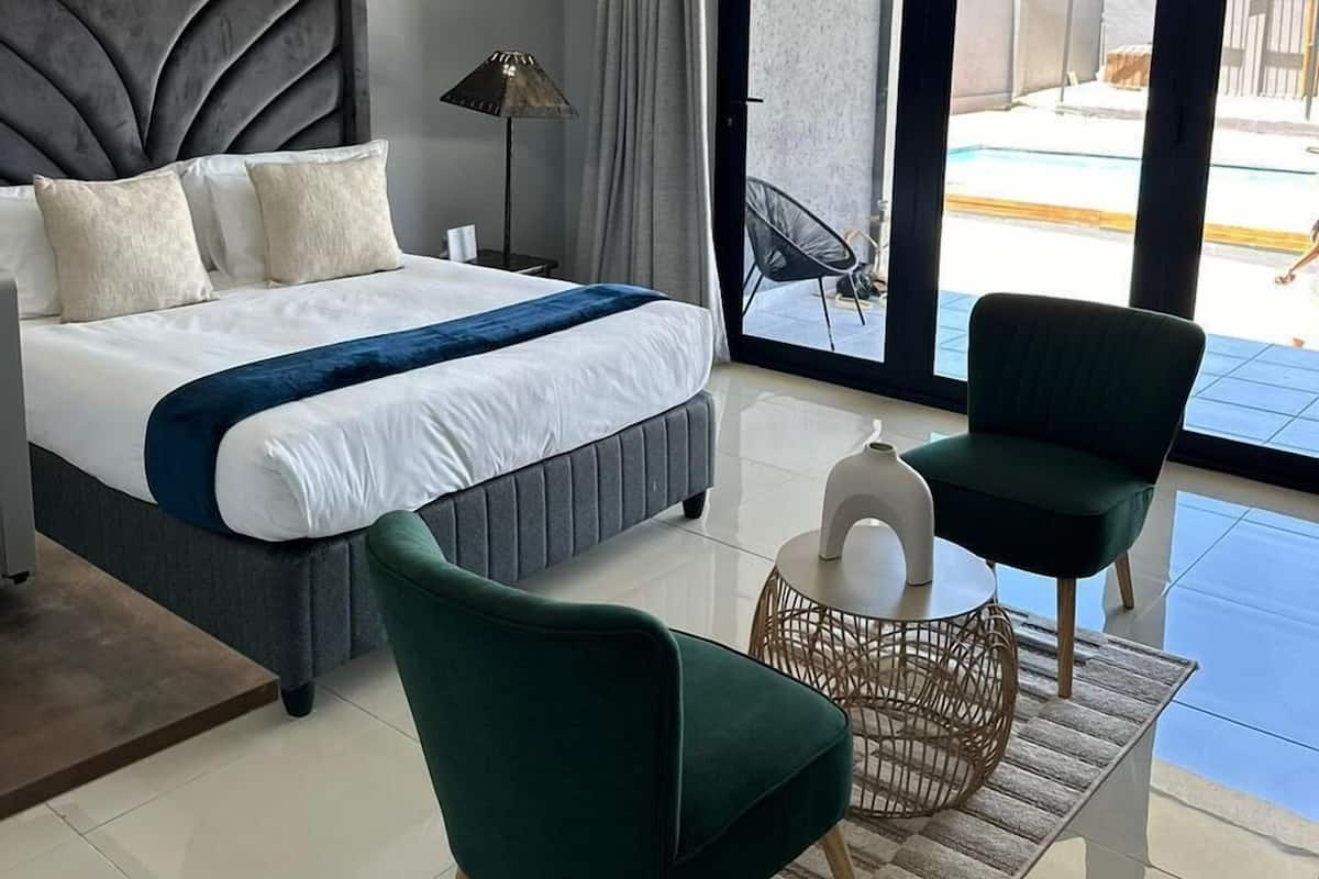 Quarto de hotel moderno com uma cama grande, uma poltrona verde, uma mesinha de apoio e vista para a piscina.