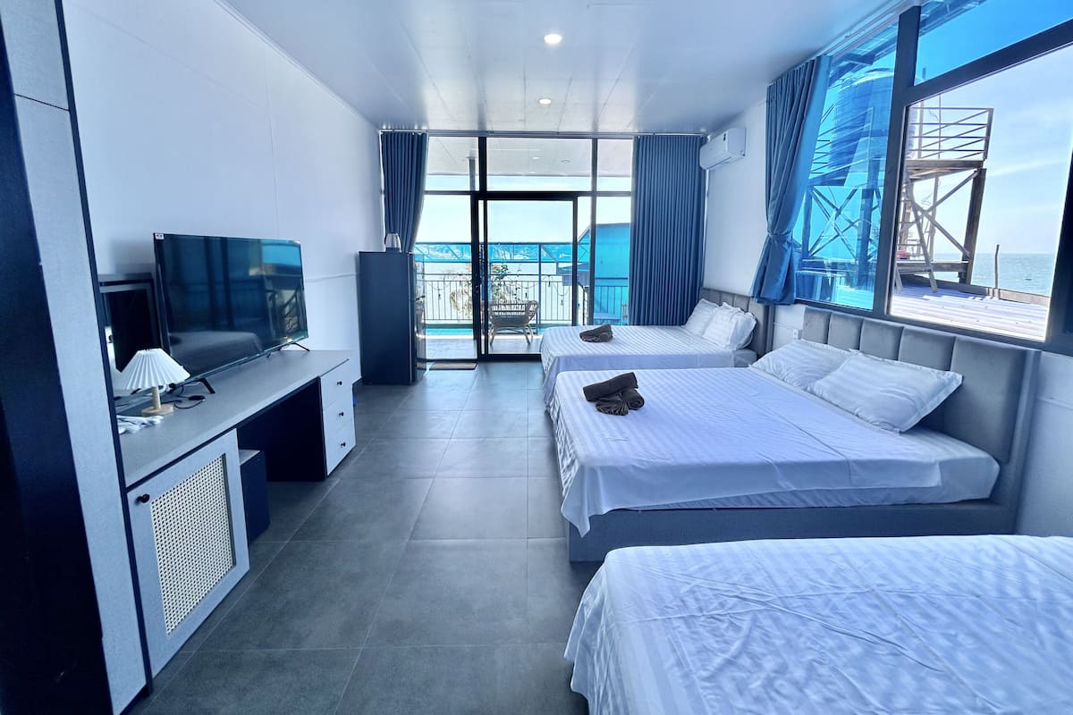 Quarto de hotel moderno com duas camas, televisão e varanda com vista para o mar.