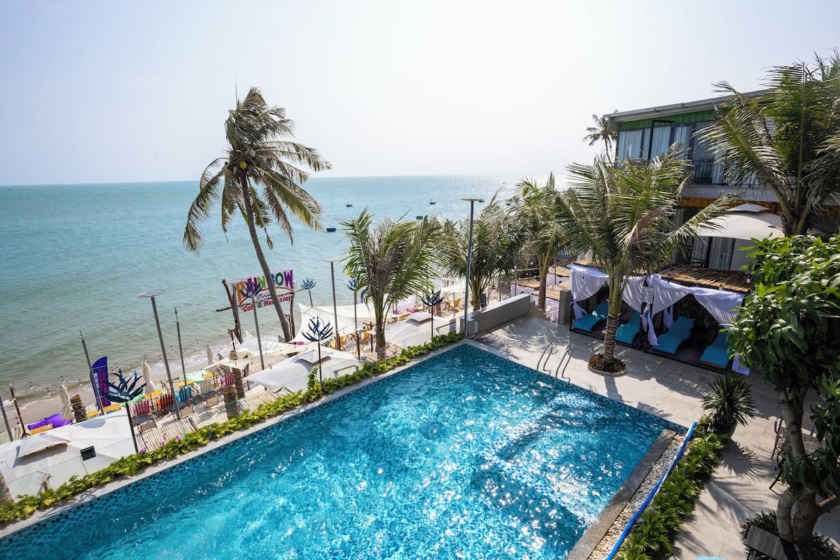 Piscina com vista para o mar, rodeada por palmeiras e espreguiçadeiras.