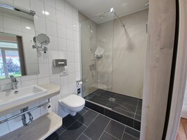 Uma casa de banho moderna com uma pia branca, sanita e zona de duche com divisória de vidro.