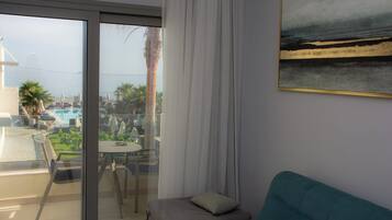 Quarto com porta de vidro deslizante para uma varanda com piscina, sofá verde-água e um quadro na parede.