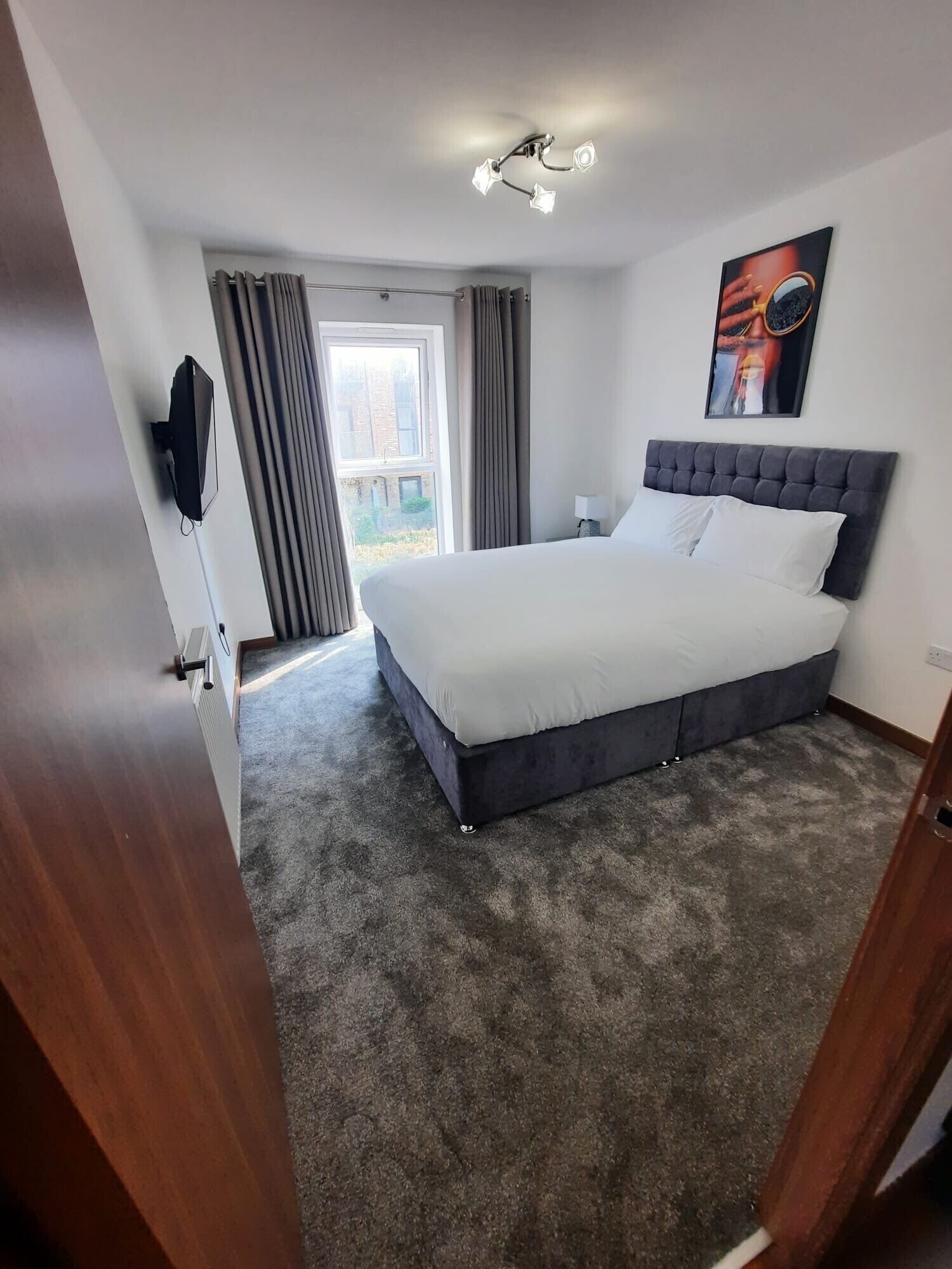Quarto com uma cama grande, televisão na parede e janela com cortinas.
