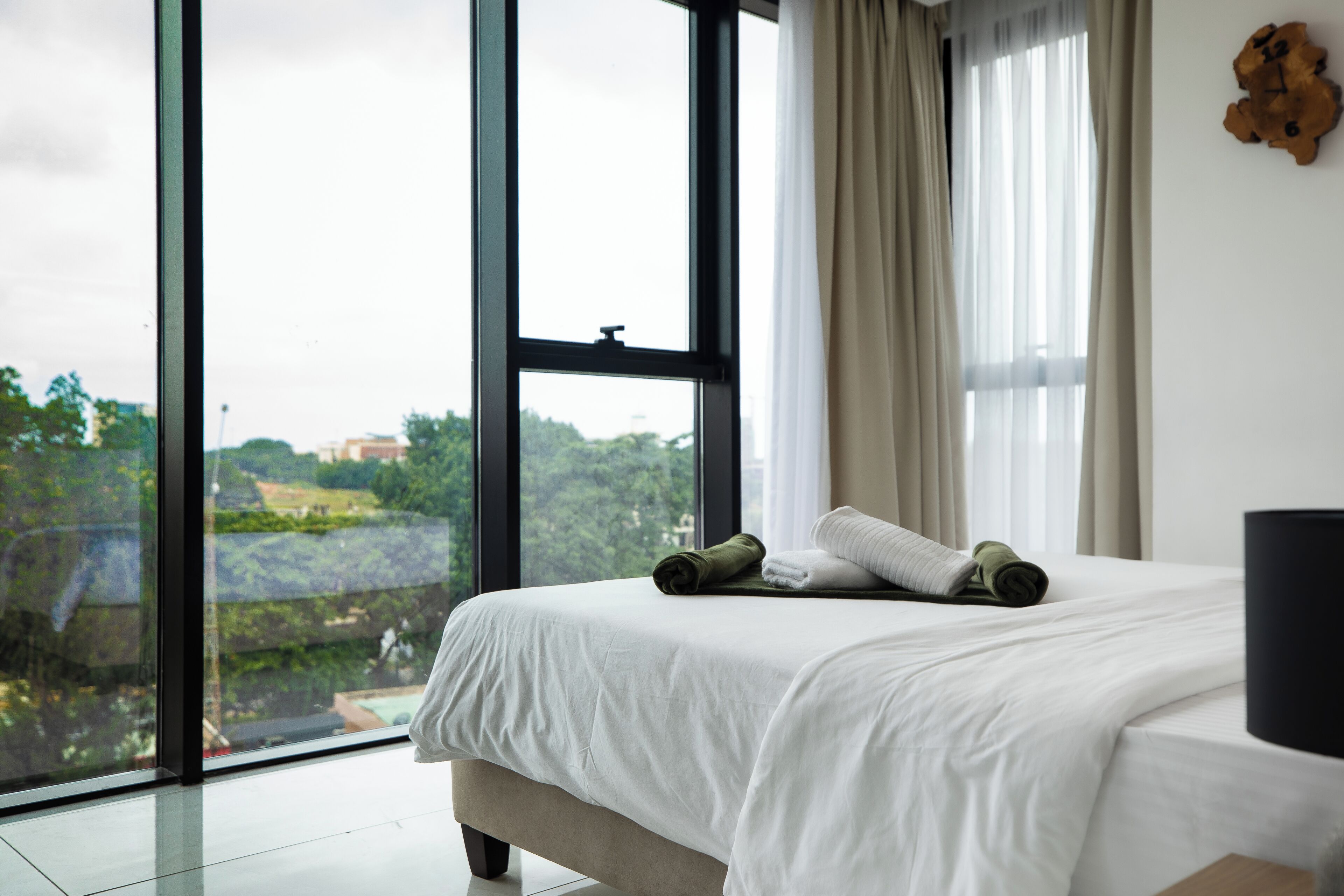 Quarto moderno com uma janela grande, cama com roupa de cama branca e vista para o verde lá fora.