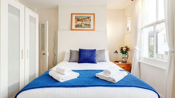 Quarto de hotel com uma cama, um quadro na parede e uma janela com cortinas.