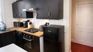 Uma cozinha compacta com armários pretos, forno embutido, geladeira e micro-ondas.