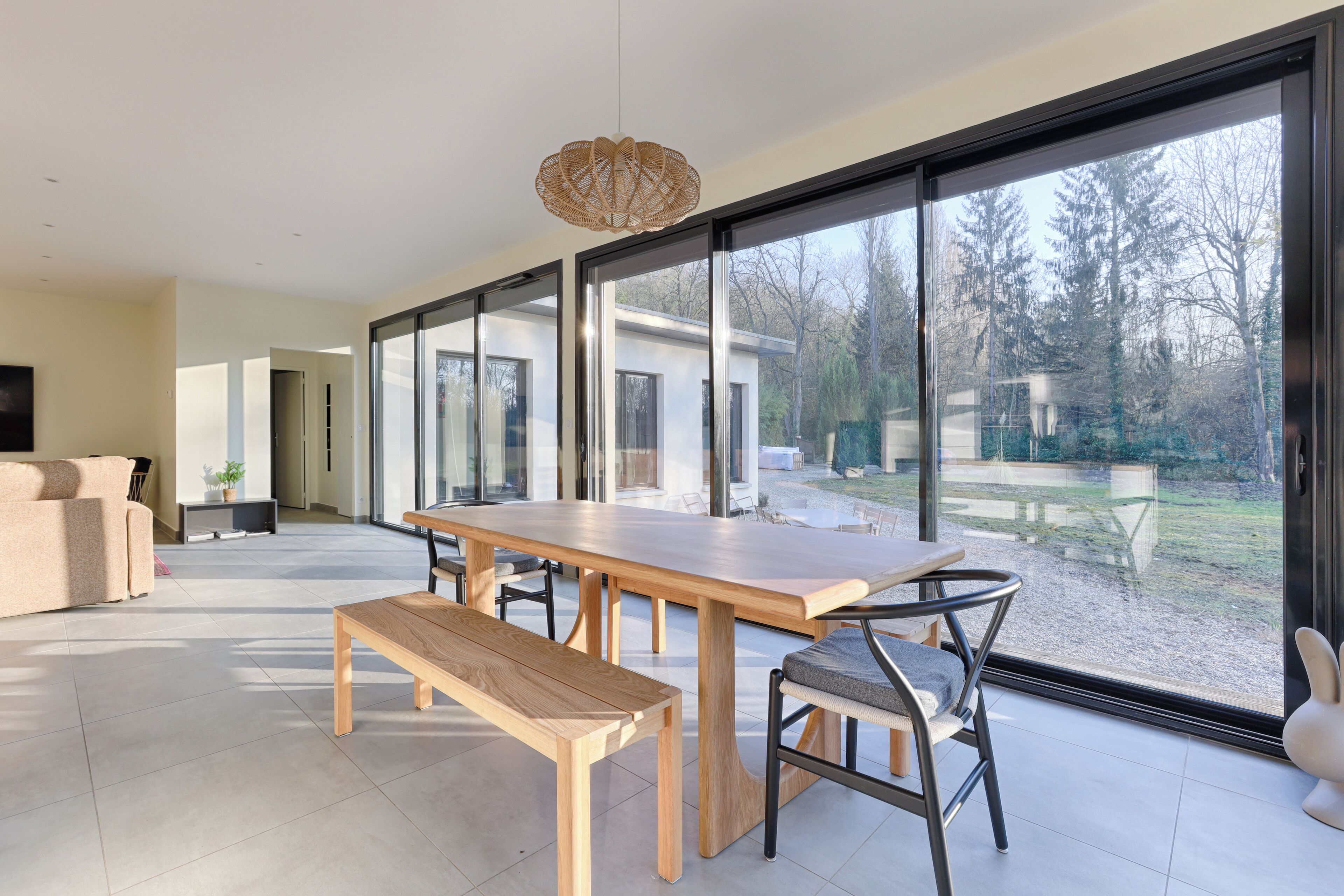 Uma sala ampla com uma grande mesa de madeira e banco, um sofá moderno e uma janela grande com vista para o exterior.