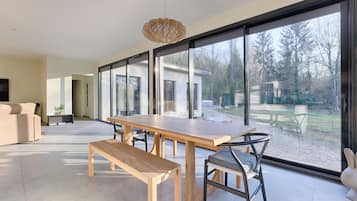Uma sala ampla com uma grande mesa de madeira e banco, um sofá moderno e uma janela grande com vista para o exterior.