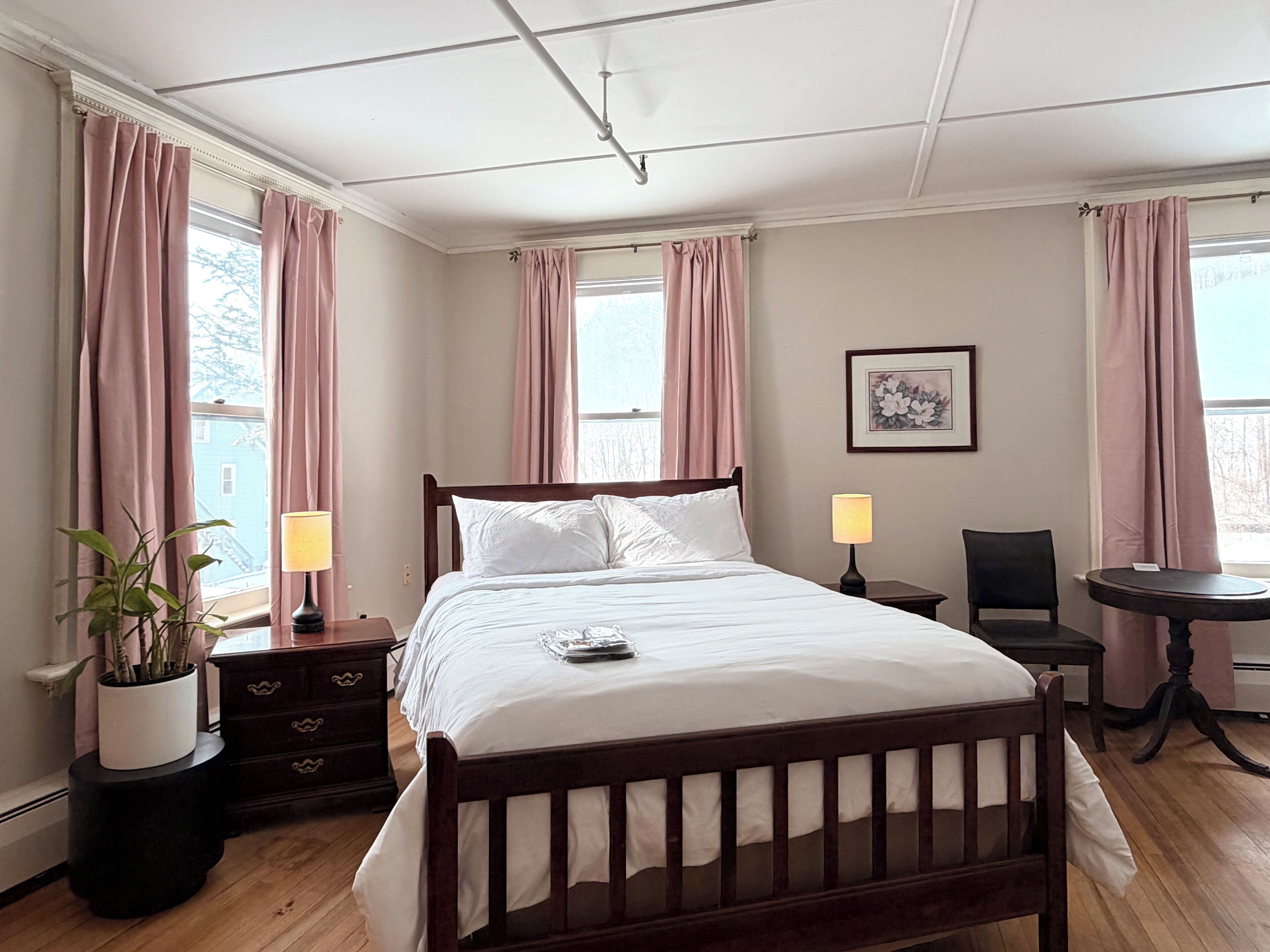 Quarto bem arrumado com cama de madeira, abajures, uma cadeira e uma pequena mesa.