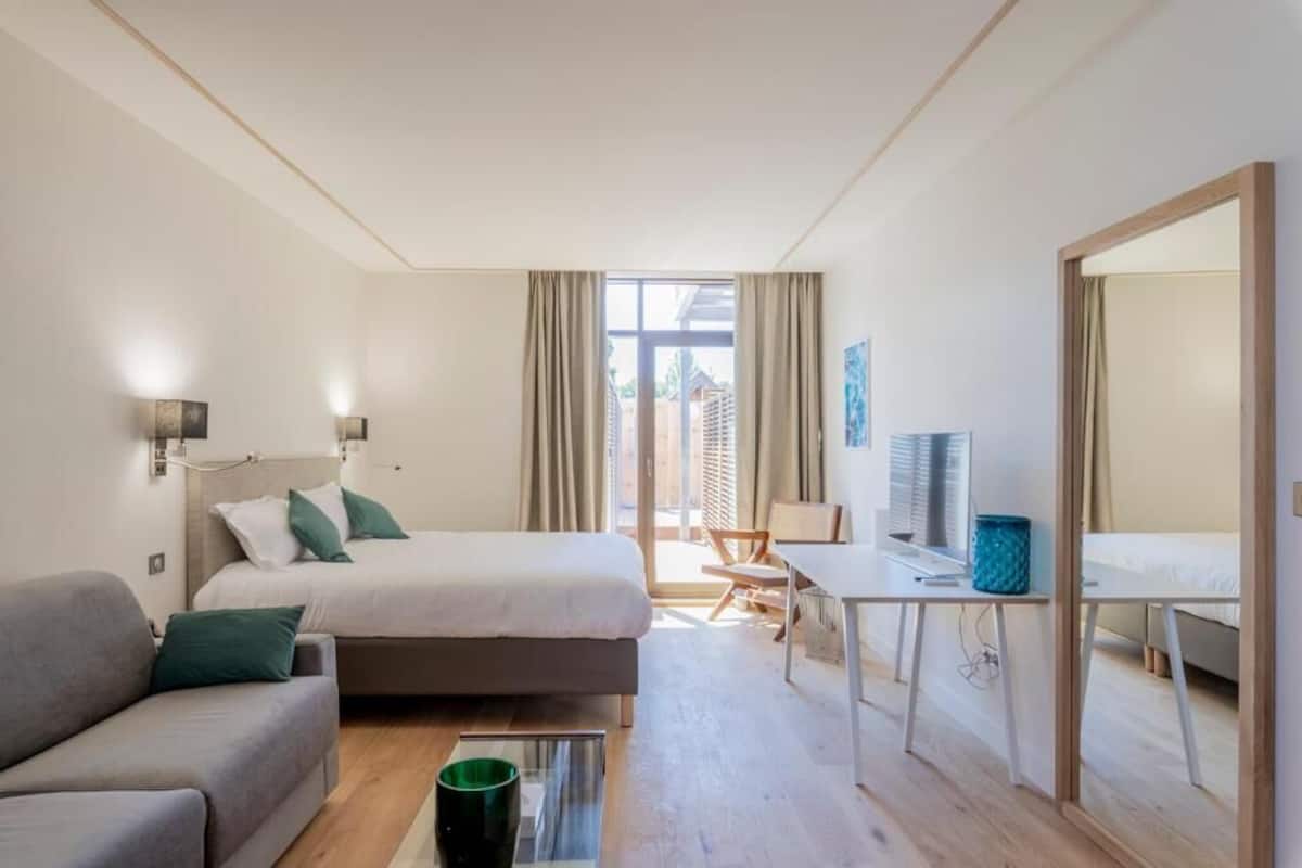 Quarto de hotel moderno com uma cama, sofá, escrivaninha e uma janela grande.