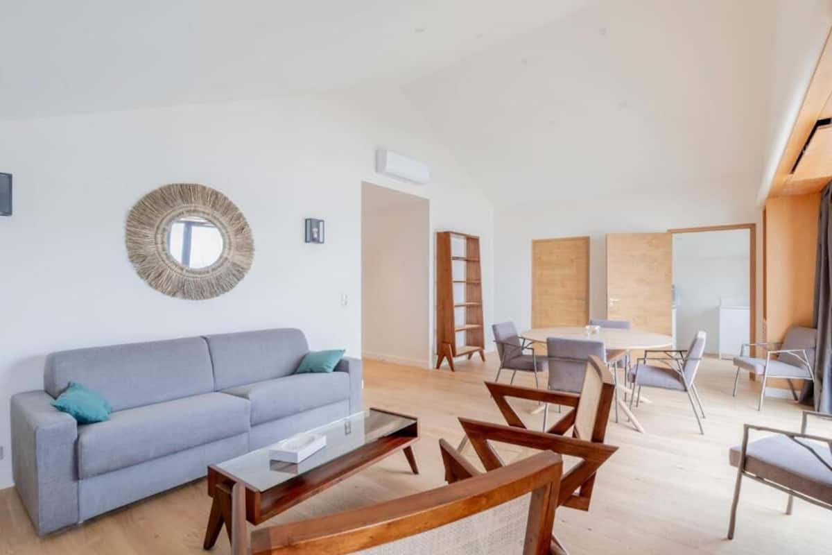 Uma sala de estar moderna com um sofá cinzento, uma mesa de centro e um espaço de jantar com cadeiras e uma mesa.