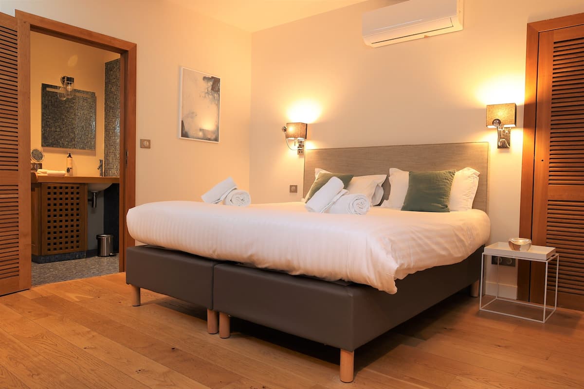 Quarto com uma cama grande, duas mesas de cabeceira, ar-condicionado na parede e piso de madeira.